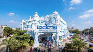 Entrada de um parque temático de neve em ambiente interno, com uma grande placa, uma multidão de pessoas e um céu azul límpido.