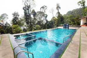 Uma piscina retangular com água azul cristalina, rodeada por um deck de pedra e uma faixa de grama.