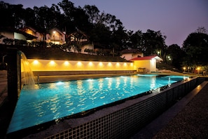 Piscina com borda azulejada, rodeada por um muro baixo com luzes uniformemente espaçadas.