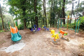 Um parquinho com diversos equipamentos, incluindo um escorregador, balanços e um carrinho de brinquedo.