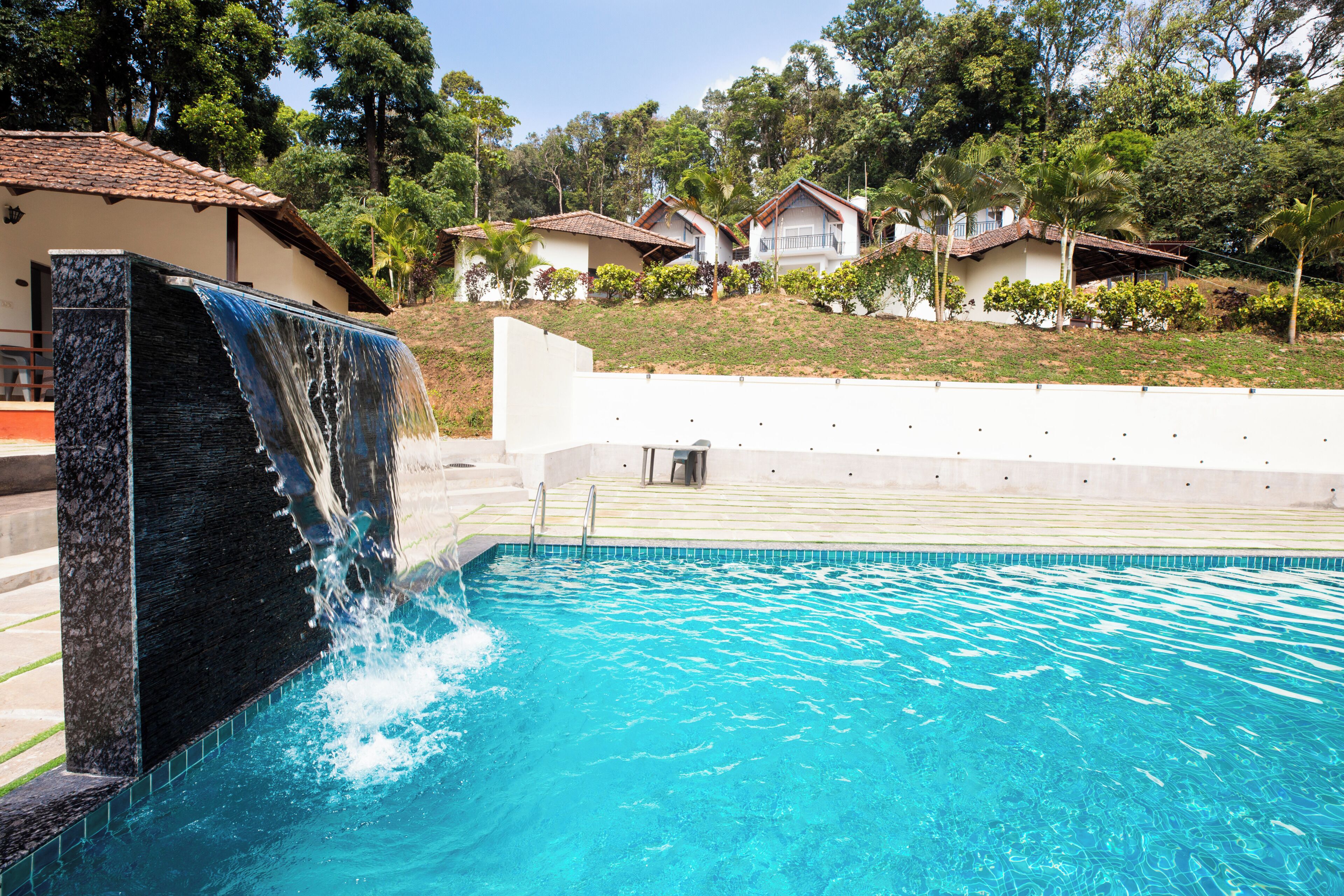 Uma piscina com cascata, rodeada por um jardim paisagístico e casas ao fundo.