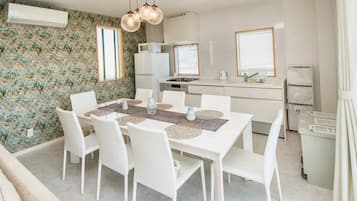 Cozinha compacta com eletrodomésticos brancos, área de refeições com mesa e cadeiras brancas, e parede com padrão.