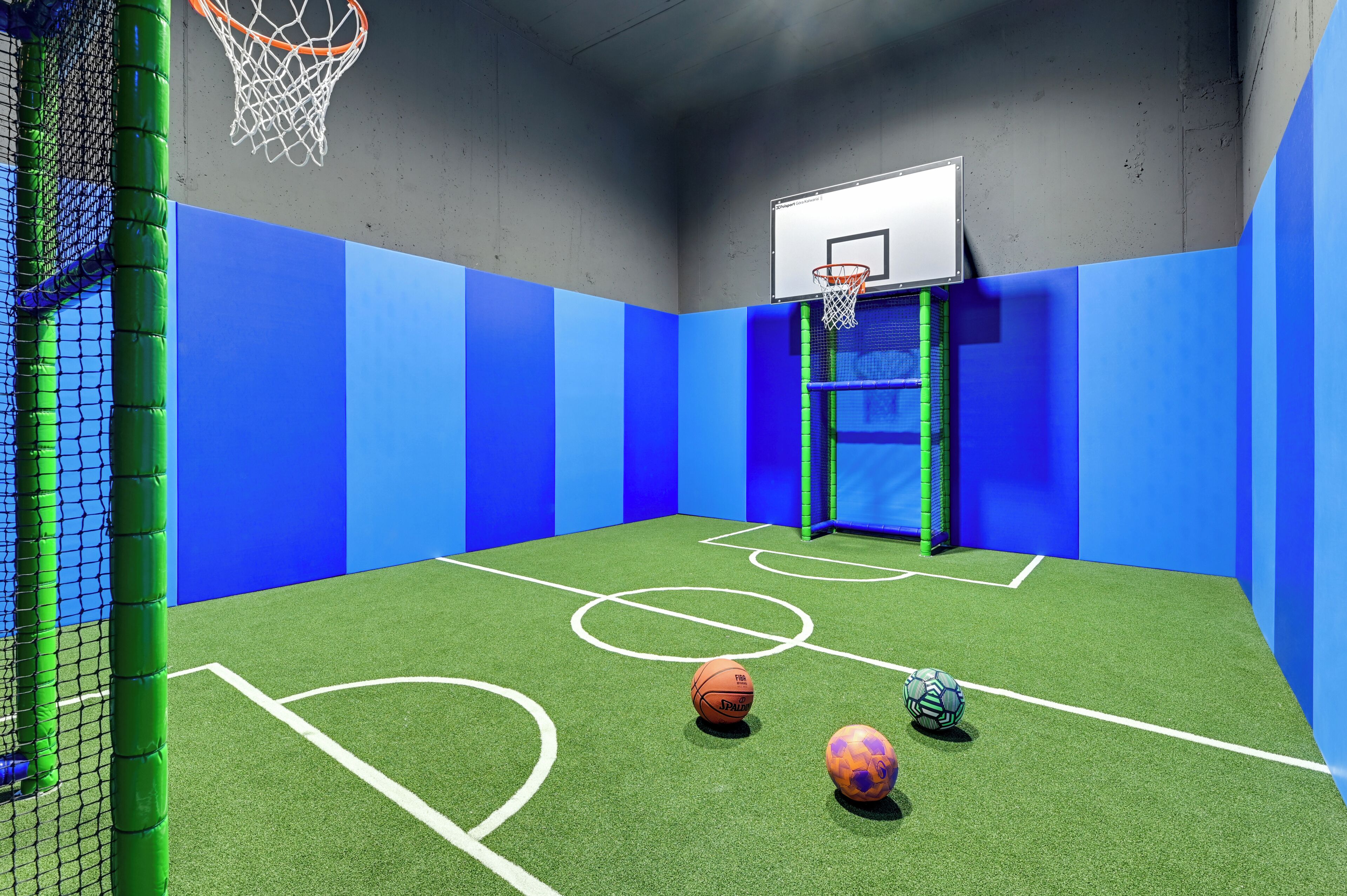 Um espaço para atividades esportivas em ambiente interno, com quadra de basquete, uma cesta de basquete com rede e duas bolas.