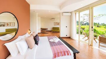 Quarto com cama, um banquinho, área de refeições e vista para uma paisagem verde.