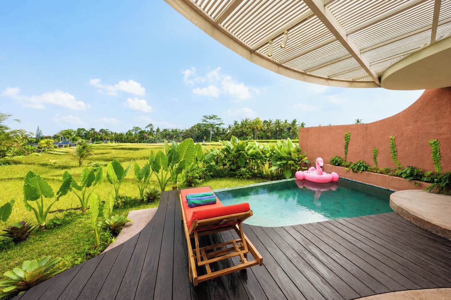 Uma área de piscina com deck de madeira, uma cadeira de lounge e um boi de flamingo flutuante.