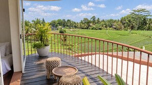 Uma varanda com vista para um campo verde e um prédio branco ao longe.