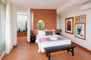 Quarto de hotel com cama, mesas de cabeceira, espelho redondo, obras de arte na parede e um banco.