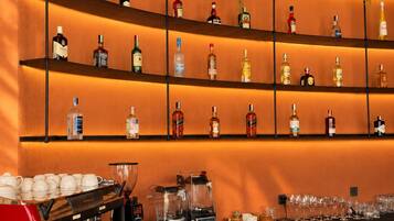 Uma área de bar com prateleiras de garrafas de bebidas, uma máquina de café e um balcão com copos e xícaras.