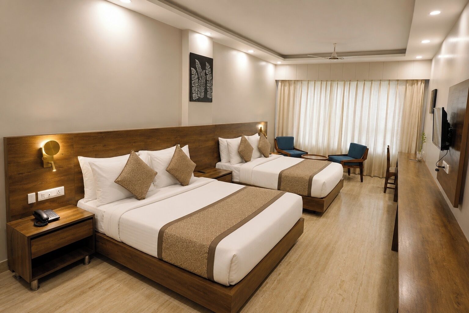 Quarto de hotel com duas camas, uma escrivaninha, uma cadeira e uma televisão.