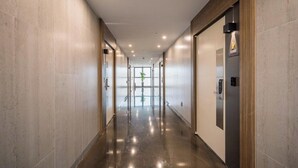 Corredor moderno de hotel com piso lustroso, portas de vidro e um elevador visível à direita.