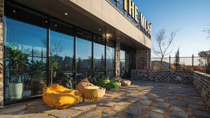 Um edifício com fachada de vidro ampla, área externa com assentos acolchoados e um pátio com piso de pedra.