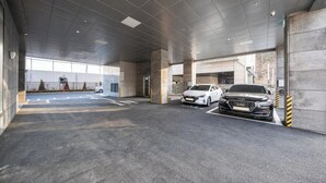 Um estacionamento com dois carros estacionados, paredes de concreto e teto com azulejos quadrados.