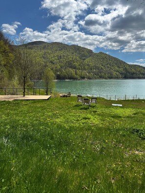 Um parque à beira de um lago, com gramado, alguns bancos e vista para o lago e colinas arborizadas.