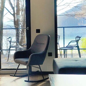 Quarto moderno com uma cadeira de balanço, um sofá e vista para o exterior através de grandes janelas.
