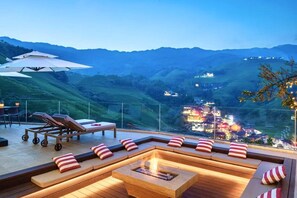 Terraço no telhado com lareira, área de estar e vista para um vale iluminado à distância.