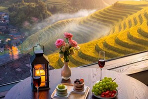Uma mesa com uma vela, um vaso de flores, um copo de vinho, uma sobremesa e uma taça de uvas.