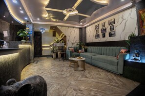Um lobby moderno com um balcão de recepção, um sofá verde, uma pequena mesa redonda e uma estátua de Buda.