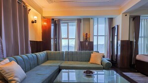 Uma sala de estar moderna com um sofá seccional, uma mesa de centro de vidro e vista para o exterior por grandes janelas.