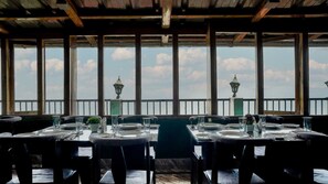 Restaurante com vista para o horizonte urbano, apresentando uma longa mesa posta para refeição.