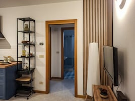 Uma cozinha com uma estante de metal preto, uma porta de madeira que dá para um banheiro e uma televisão sobre um suporte de madeira.