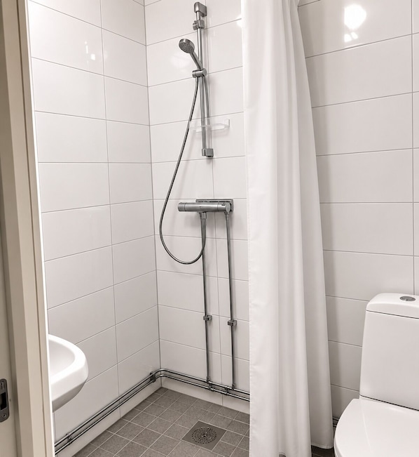 Um banheiro com azulejos brancos, chuveiro com barra e vaso sanitário, e cortina branca.