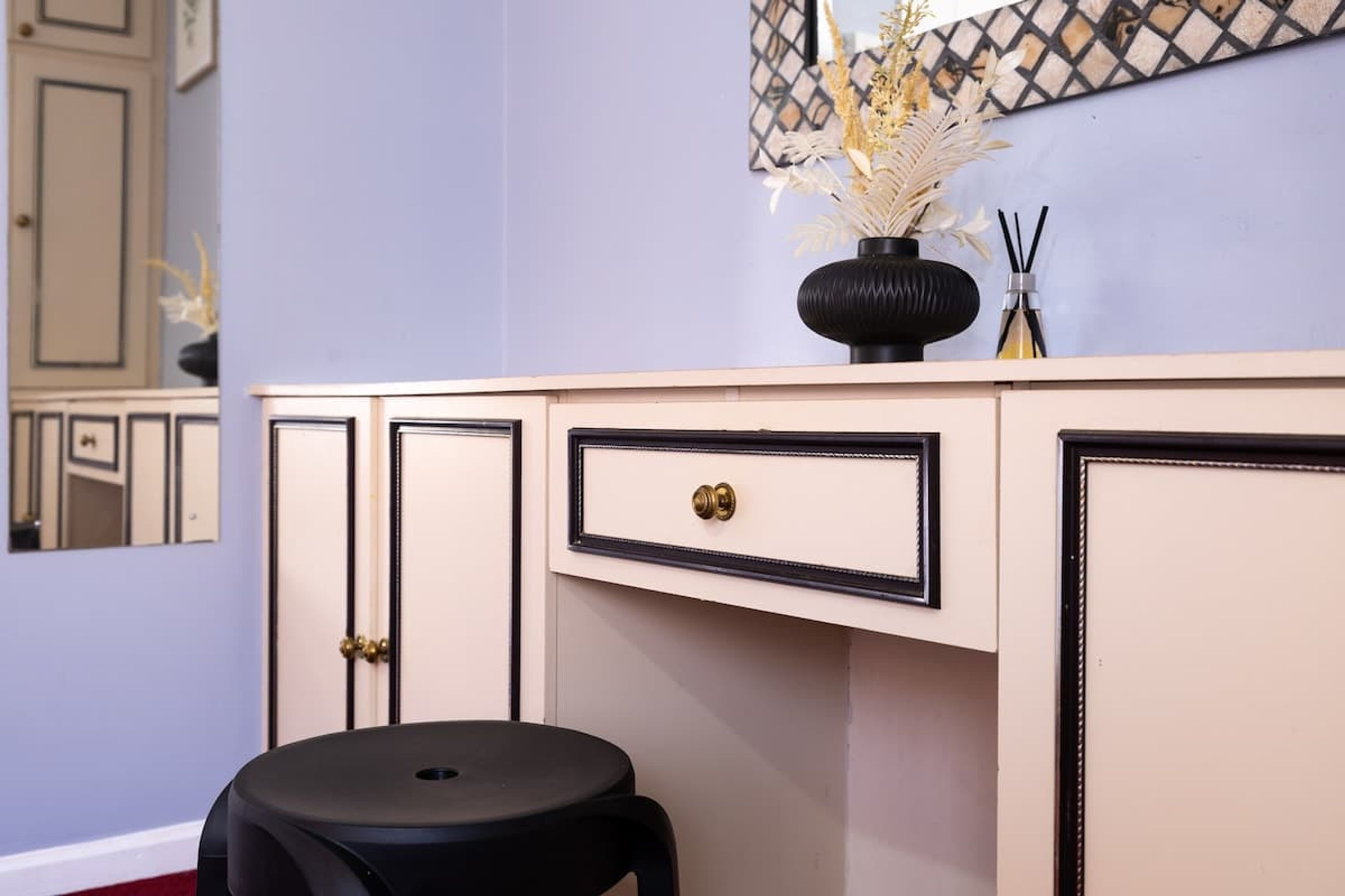 Um quarto com um armário claro, um banquinho redondo e um vaso decorativo com plantas secas no topo.