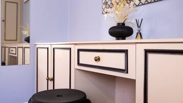 Um quarto com um armário claro, um banquinho redondo e um vaso decorativo com plantas secas no topo.