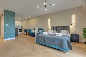 Quarto de hotel moderno com uma cama grande, uma mesa de trabalho e uma cozinha compacta.