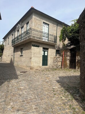 Um edifício de pedra com varanda e porta verde, com a placa 'CASA JOÃO FIDALGO'.