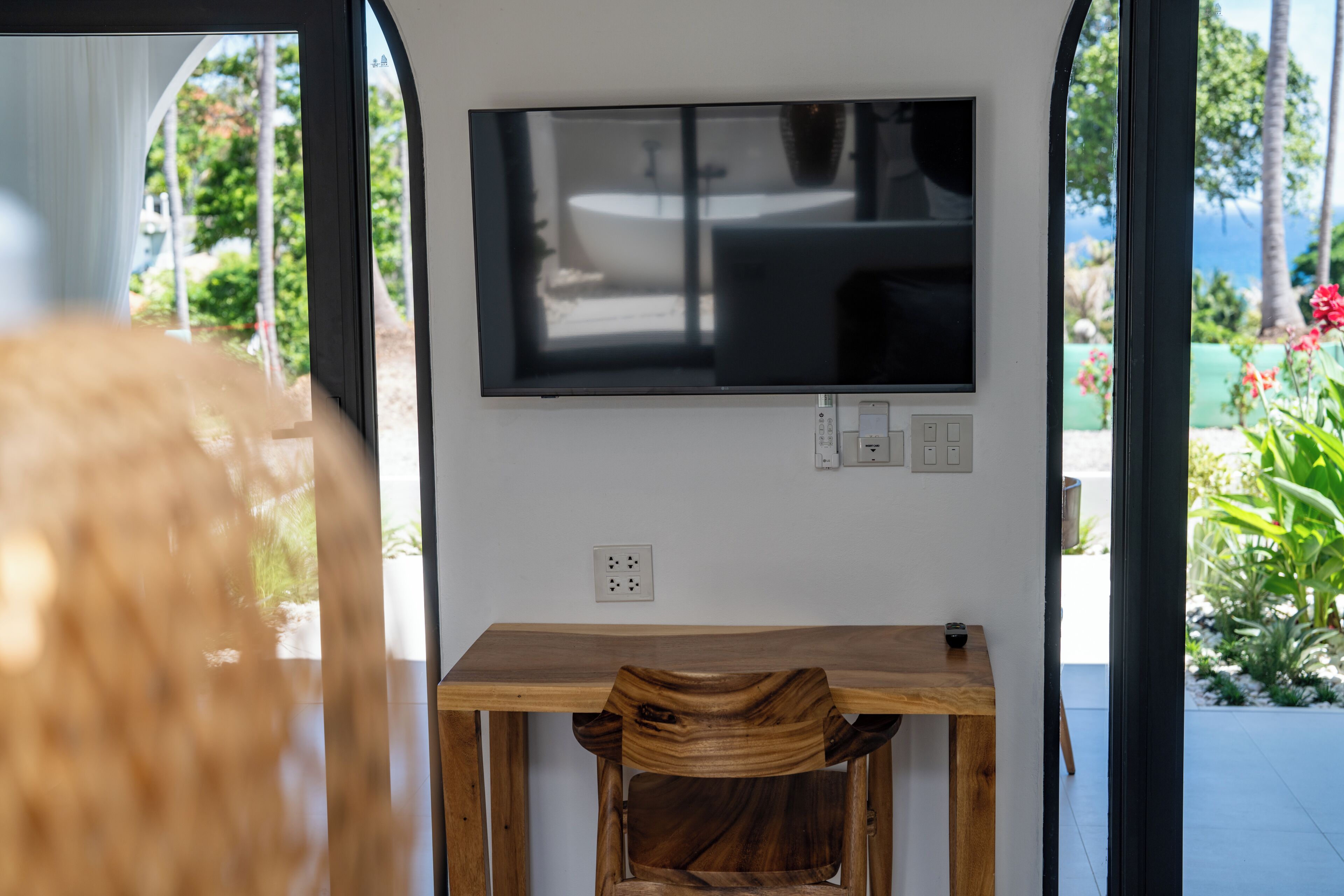 Quarto com uma mesa de madeira, televisão de tela plana na parede e vista para o verde lá fora.