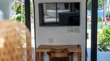 Quarto com uma mesa de madeira, televisão de tela plana na parede e vista para o verde lá fora.