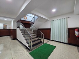 Um saguão de hotel com escadas, um extintor de incêndio e um tapete verde.