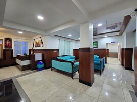 Um saguão de hotel com balcão de recepção, área de estar com sofás e um corredor que dá para outros quartos.