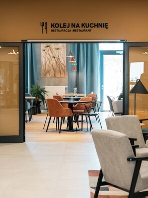 Interior de restaurante com área de refeições, cadeiras, mesa e um letreiro sobre a entrada.