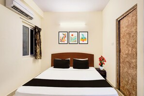 Quarto de hotel com cama, mesa de cabeceira, planta em vaso e três quadros na parede.