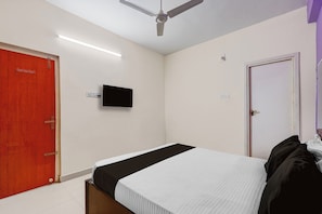 Um quarto com cama, ventilador de teto, televisão e porta.