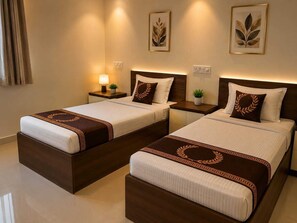 Quarto de hotel com duas camas, cada uma com cabeceira marrom, mesa de cabeceira com abajur e planta suspensa na parede.