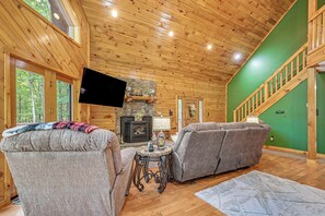 Interior acolhedor de uma cabana com lareira, paredes de madeira e uma parede de destaque verde, além de uma escada.