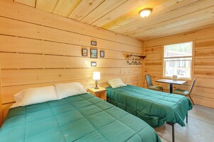 Quarto com duas camas, uma mesa, uma cadeira, um abajur e uma janela.