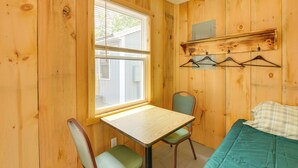 Um quarto pequeno e acolhedor com decoração em madeira, uma mesa com uma cadeira, uma cama e uma janela com persianas.