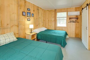 Quarto de madeira com duas camas, uma janela e ar-condicionado fixado na parede.