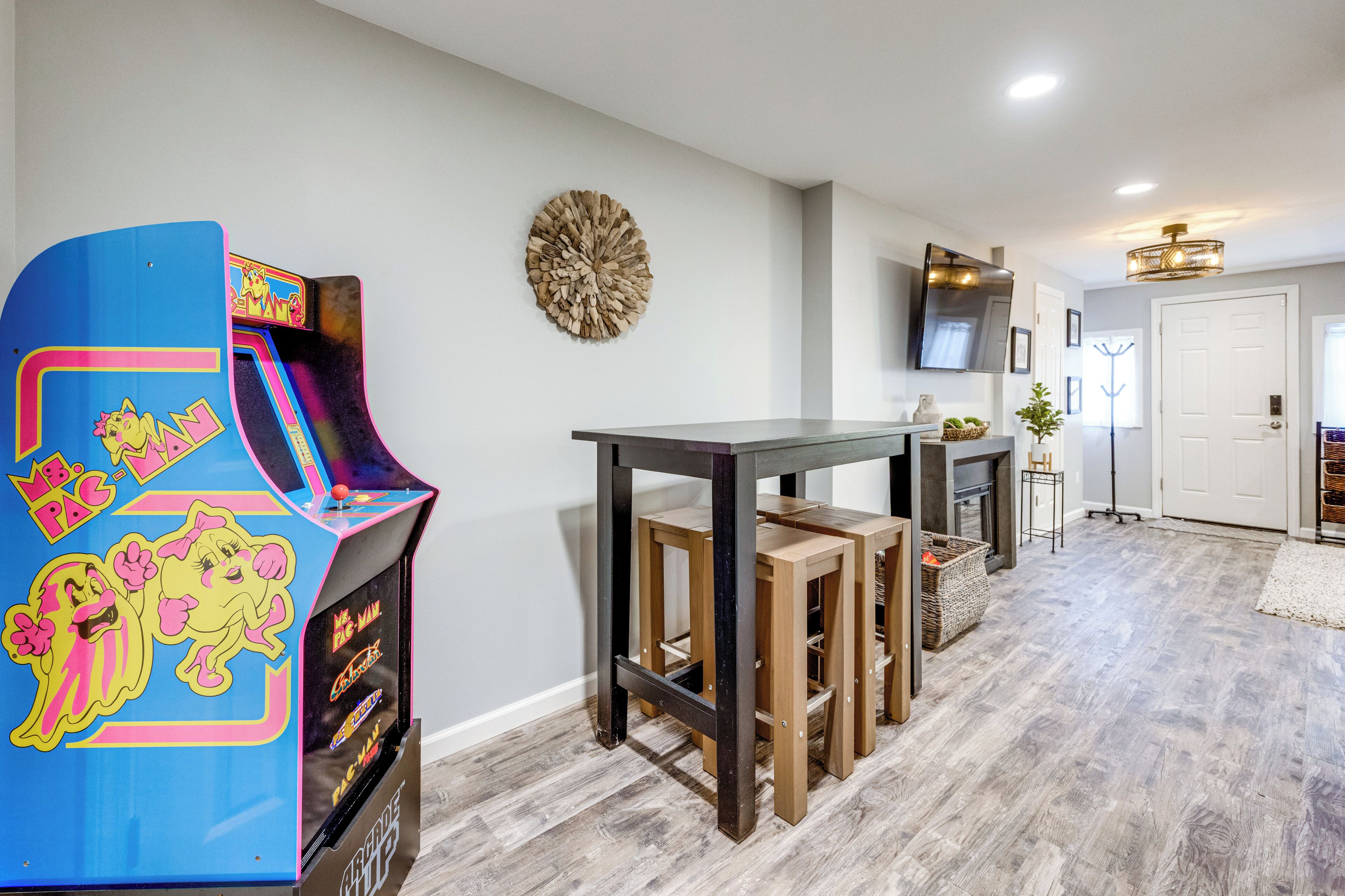 Um quarto com uma máquina de jogos eletrônicos antigos, uma mesa de madeira e uma televisão presa à parede.