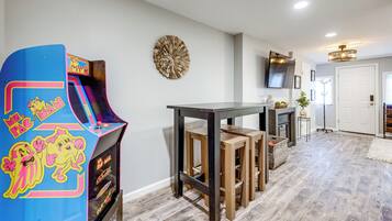 Um quarto com uma máquina de jogos eletrônicos antigos, uma mesa de madeira e uma televisão presa à parede.