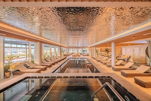 Um spa moderno com piscina central, áreas de descanso e amplas janelas com vista para o porto de iates.