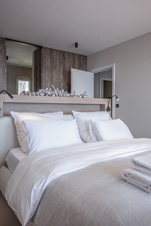 Quarto moderno com cama grande, cabeceira de madeira, espelho e luminária fixada na parede.