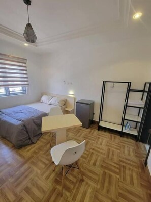Quarto compacto com cama, secretária pequena, cadeira, guarda-roupa e radiador.