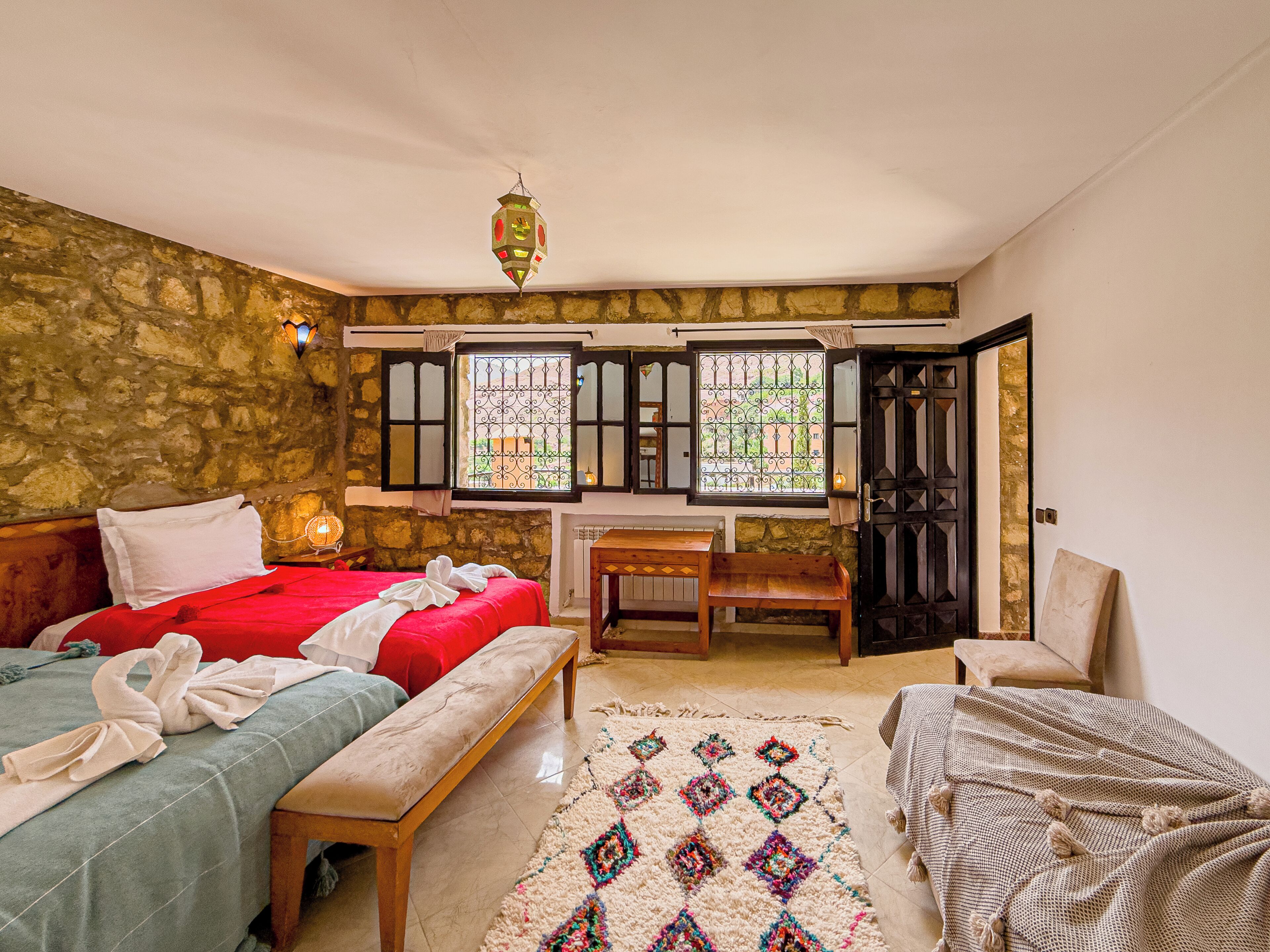 Quarto com duas camas, um banco, uma mesa e um tapete estampado.