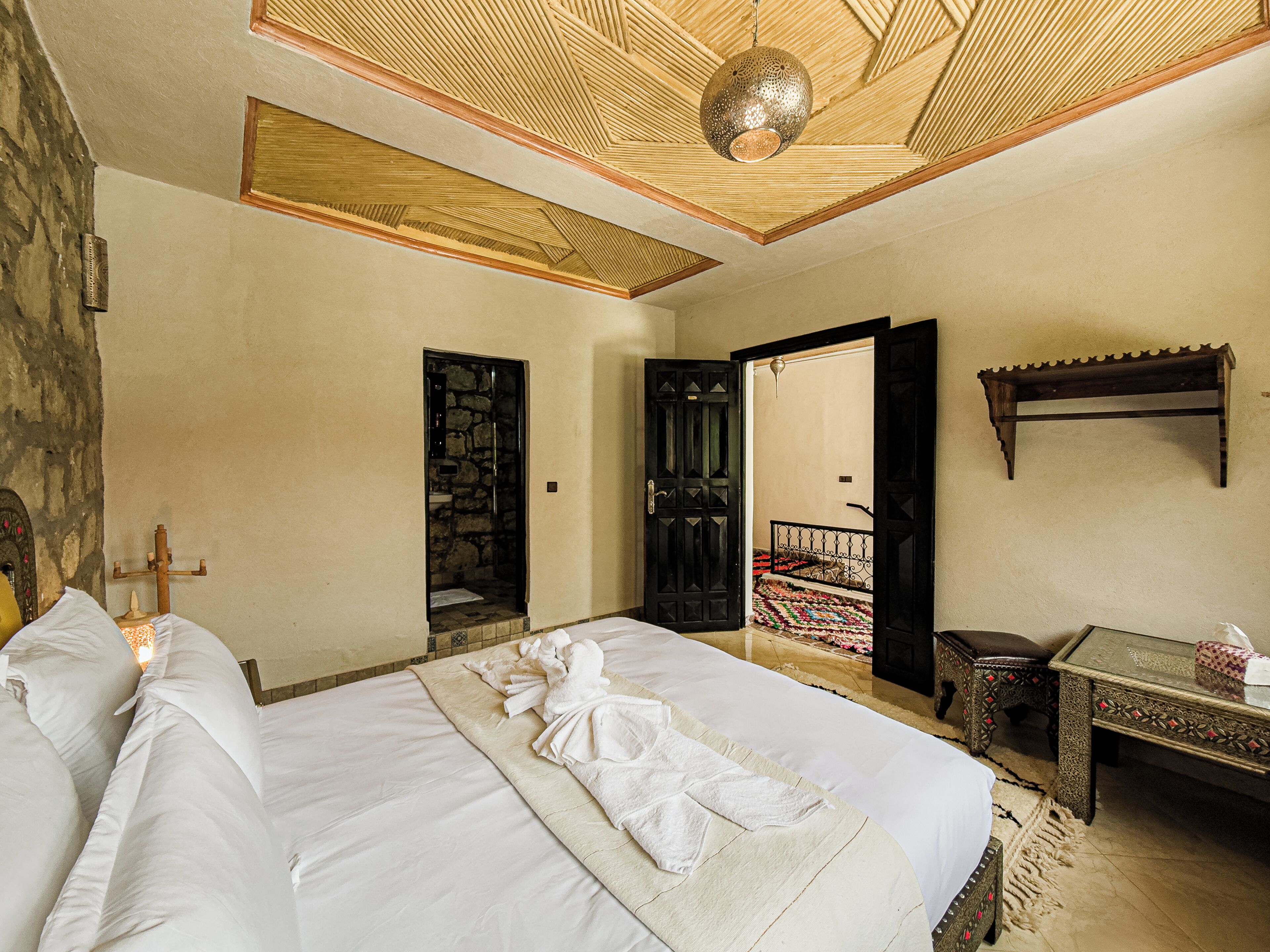 Quarto de hotel com cama, uma mesa pequena, um espelho e teto com um padrão decorativo.