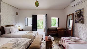 Quarto de hotel com duas camas, um banquinho, uma mesa pequena, um espelho e vista para o exterior.