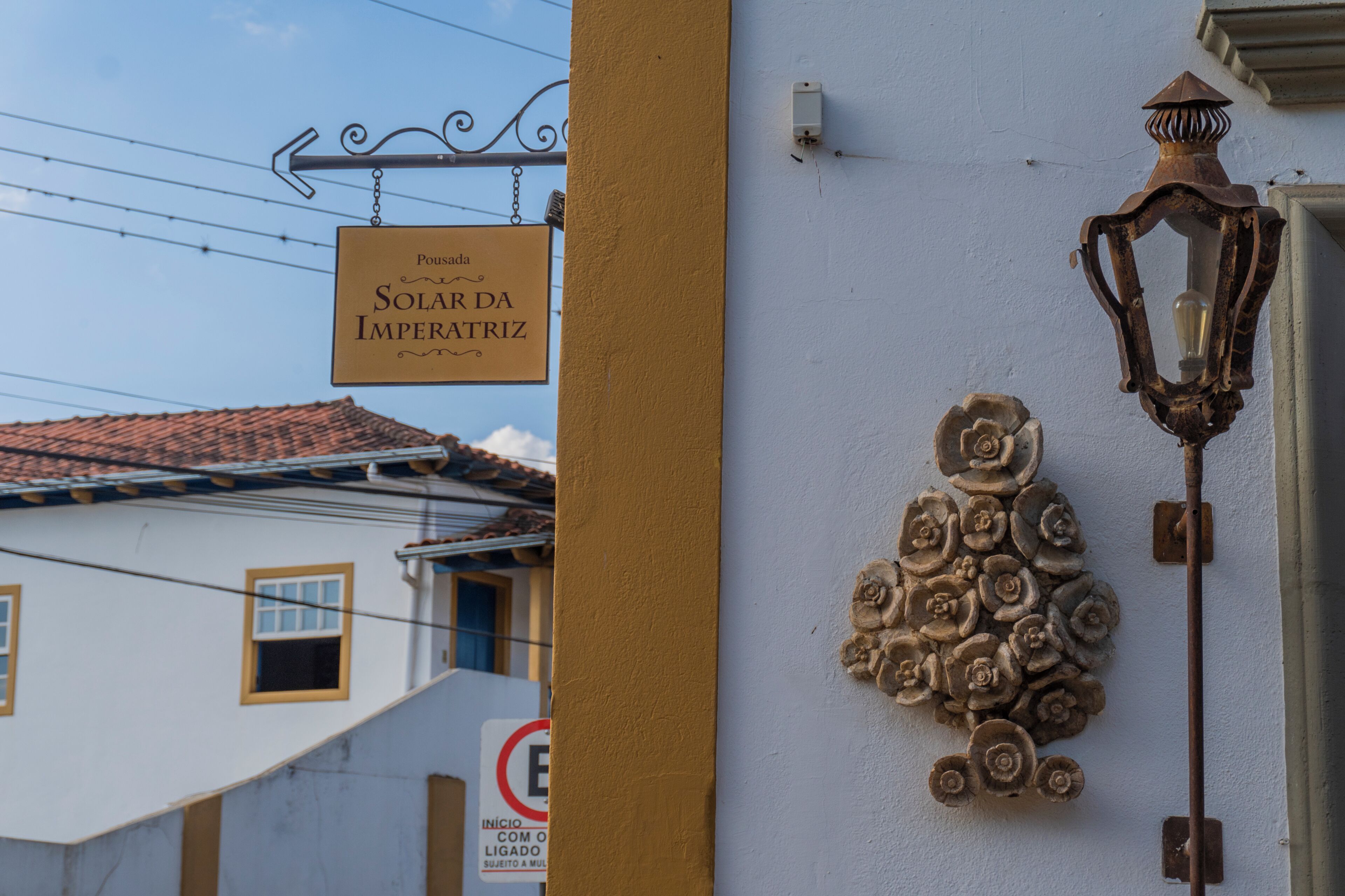 Esquina de um edifício com uma placa indicando 'Pousada Solar da Imperatriz' e uma peça de metal ornamental.